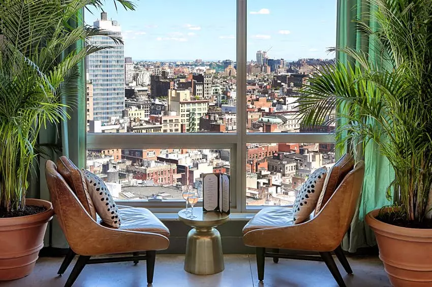 Dve stoličky vedľa okna, orámované rastlinami a zelenými závesmi; najlepšie strešné bazény v New Yorku