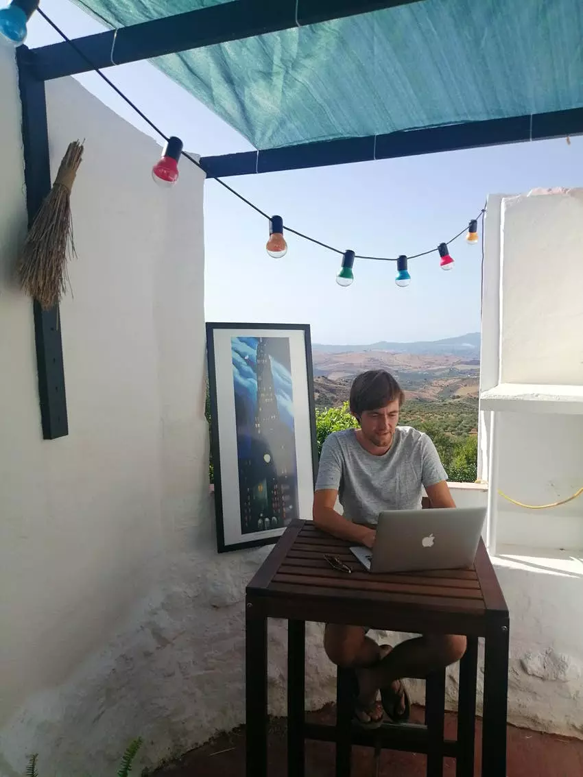 Muž sedí za stolom s notebookom. Za ním je úžasný výhľad na olivové háje. Obraz od umelkyne Georgia O'Keeffe je opretý o stenu