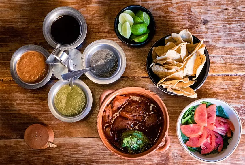 Letecký pohľad na tacos, plátky limetiek a paradajok a rôzne omáčky usporiadané na drevenom stole