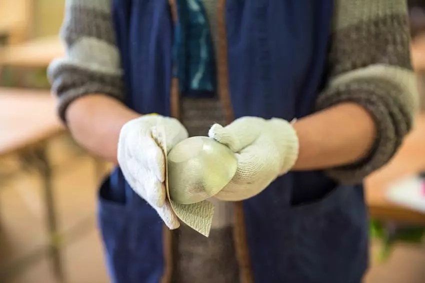 Detailný záber rúk v rukaviciach, ktoré brúsia medený pohár na saké